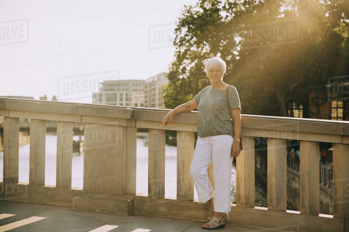 Full length portrait of senior woman standing on bridge against railing ...