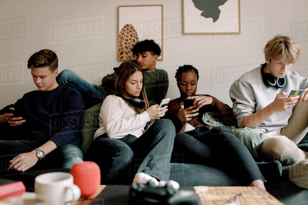 Multi-ethnic friends using social media on mobile phones while sitting ...