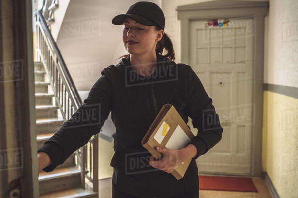 Confident delivery woman with package standing at doorstep - Stock ...