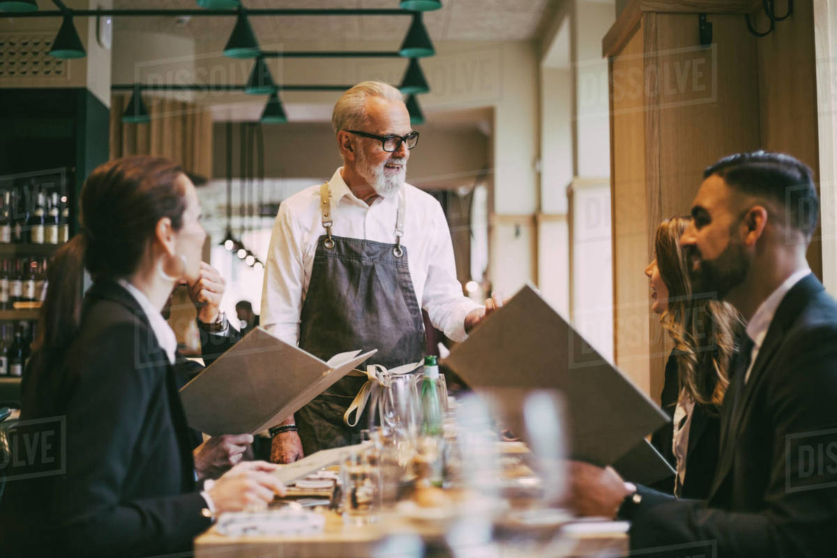 Waiter talking to business people while standing by table in restaurant ...