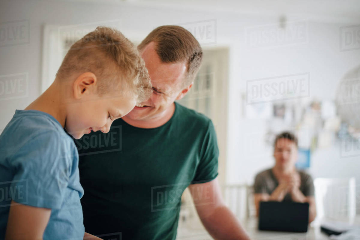 Smiling father looking at son sitting in domestic kitchen - Royalty ...