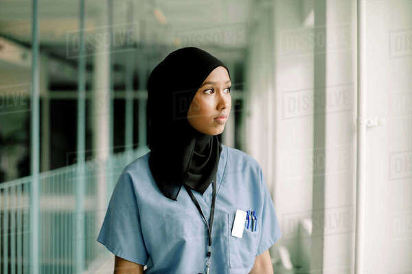 Contemplating female nurse looking through window while standing in ...