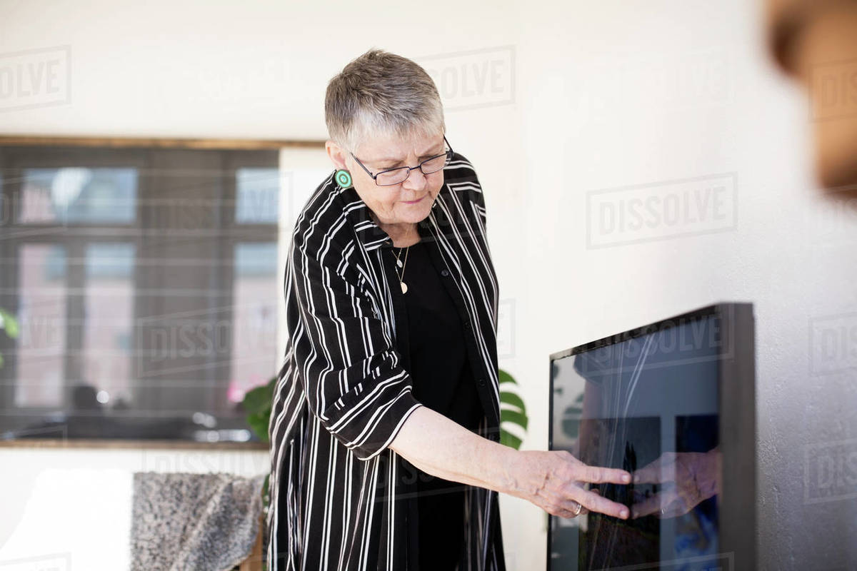 Senior woman touching television screen in living room - Royalty-free ...
