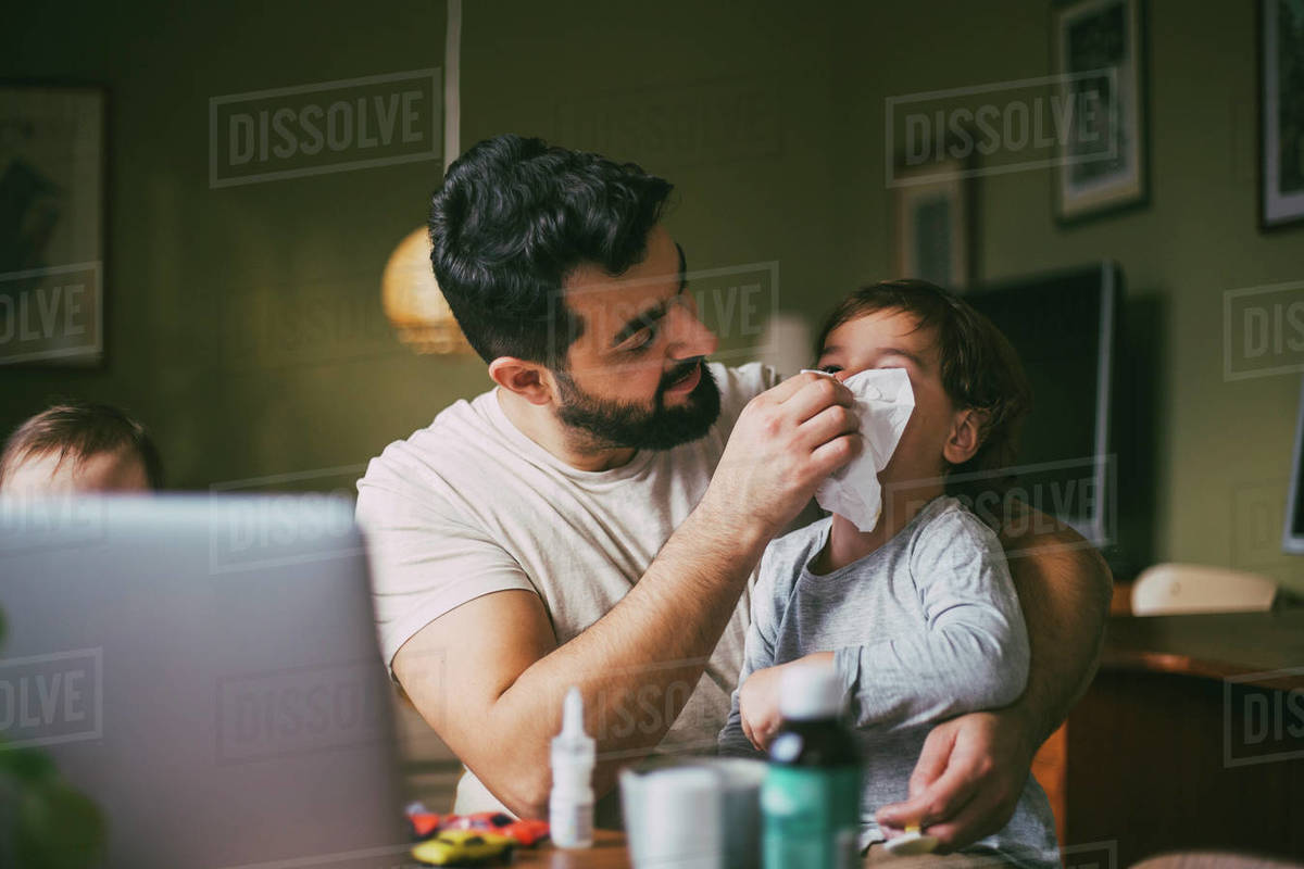 Father blowing nose of son in living room - Stock Photo - Dissolve