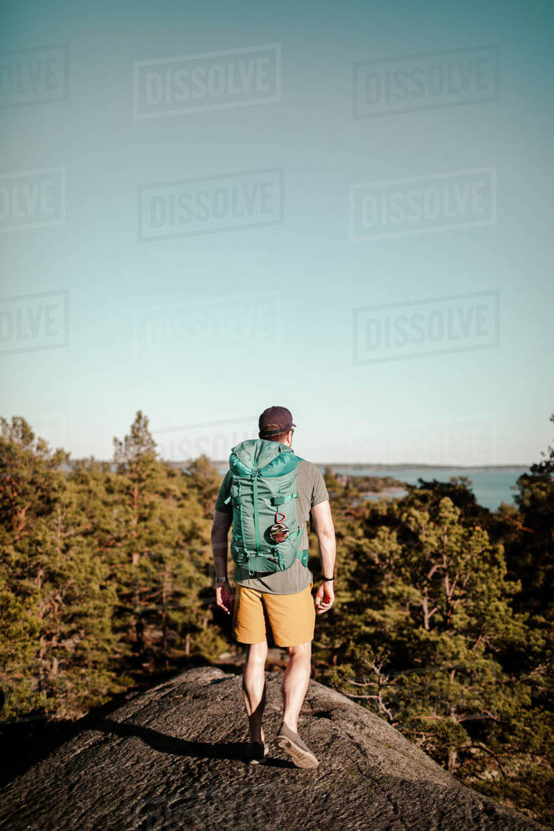 Full length rear view of male explorer standing on rock during sunny ...