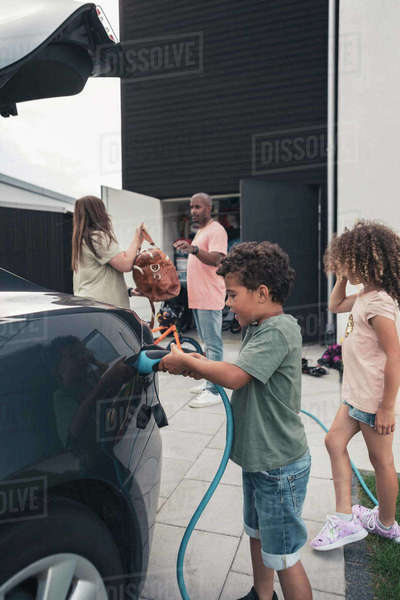 Boy charging electric car with family at front yard - Royalty-free ...