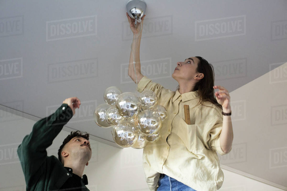 Woman hanging chandelier with boyfriend while moving in new house ...