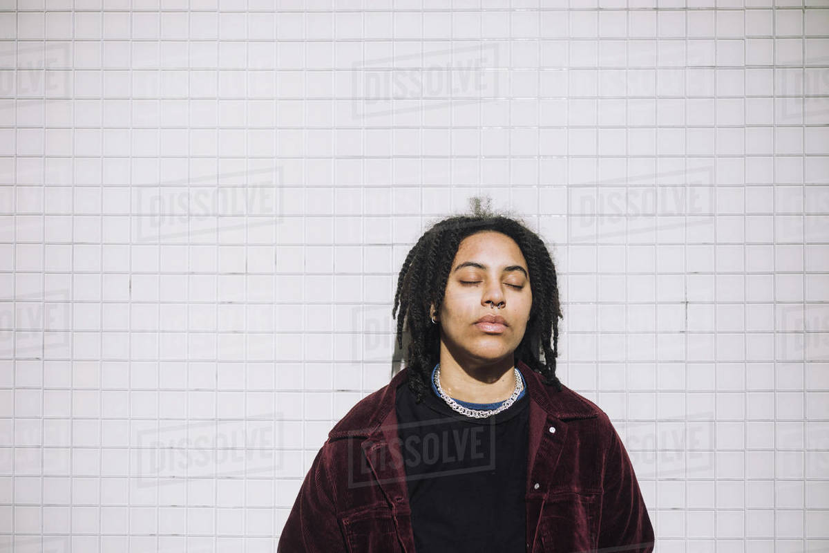 Genderqueer person with eyes closed standing in front of wall during ...