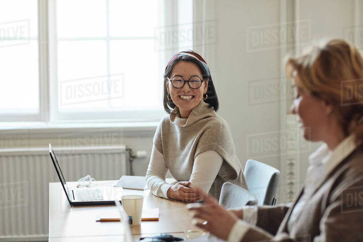 Cheerful female professor looking at colleague sitting in staffroom ...