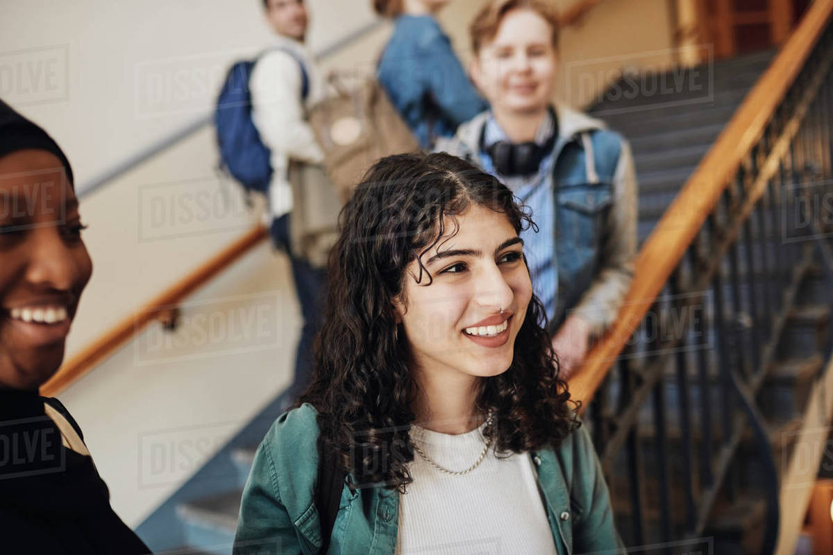 Smiling female students looking away at staircase in university ...