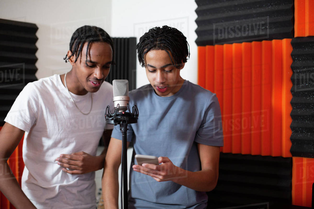 Teenage rappers sharing smart phone while recording song in studio ...