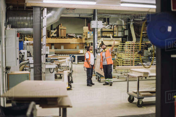 Full length of young carpenter explaining to female colleague while ...