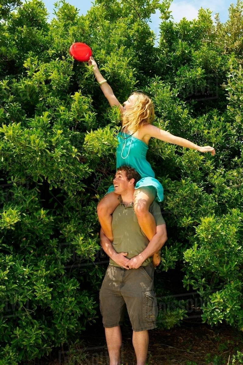 Woman sitting on man's shoulders holding - Royalty-free Stock Photo ...