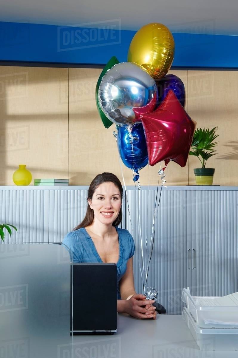 Young woman with balloons at desk - Stock Photo - Dissolve