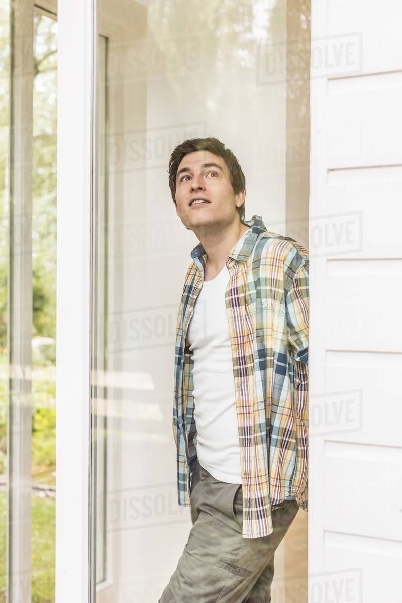 Young man gazing out of window from house - Stock Photo - Dissolve
