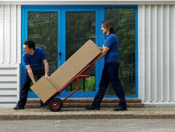 Two men carrying boxes on trolley - Stock Photo - Dissolve