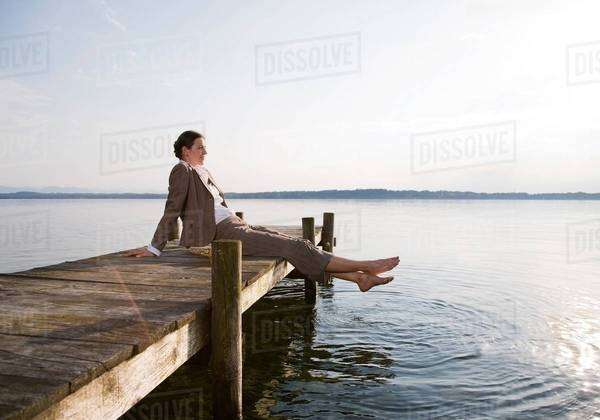 Woman sitting on pier at lake - Royalty-free Stock Photo | Dissolve