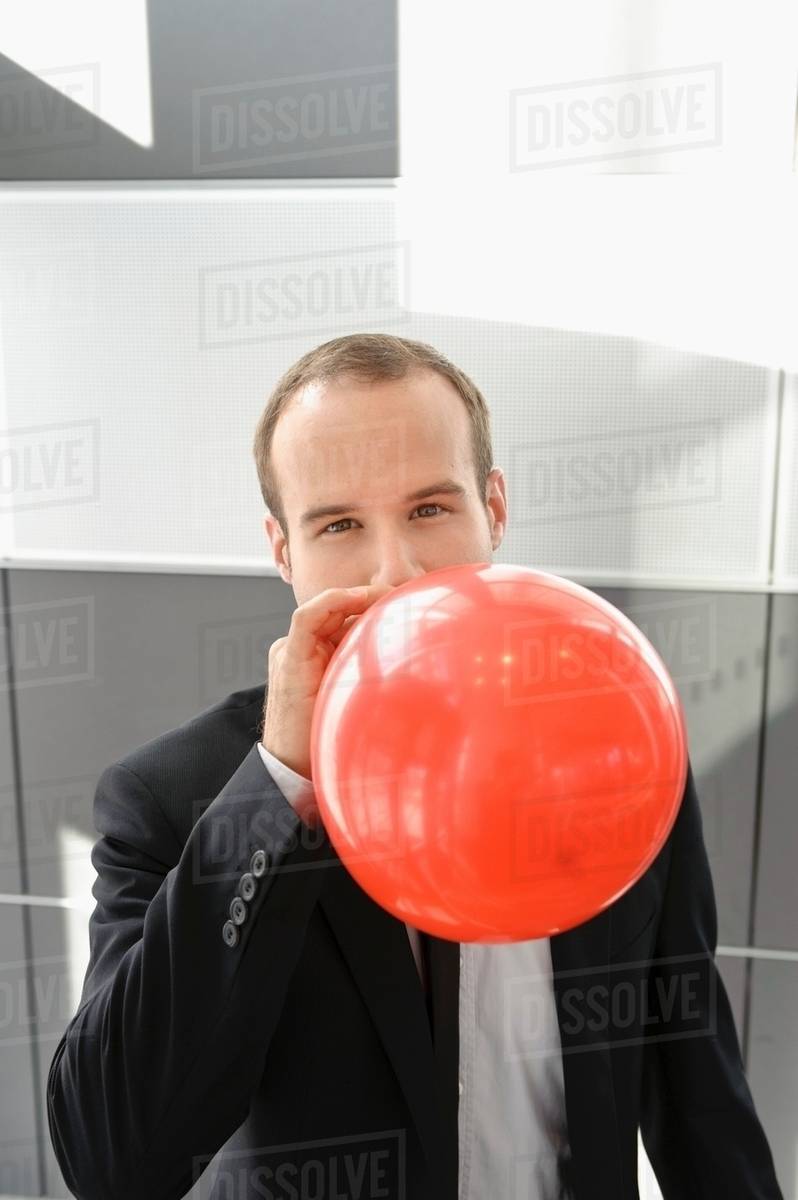 Businessman blowing up red balloon - Stock Photo - Dissolve