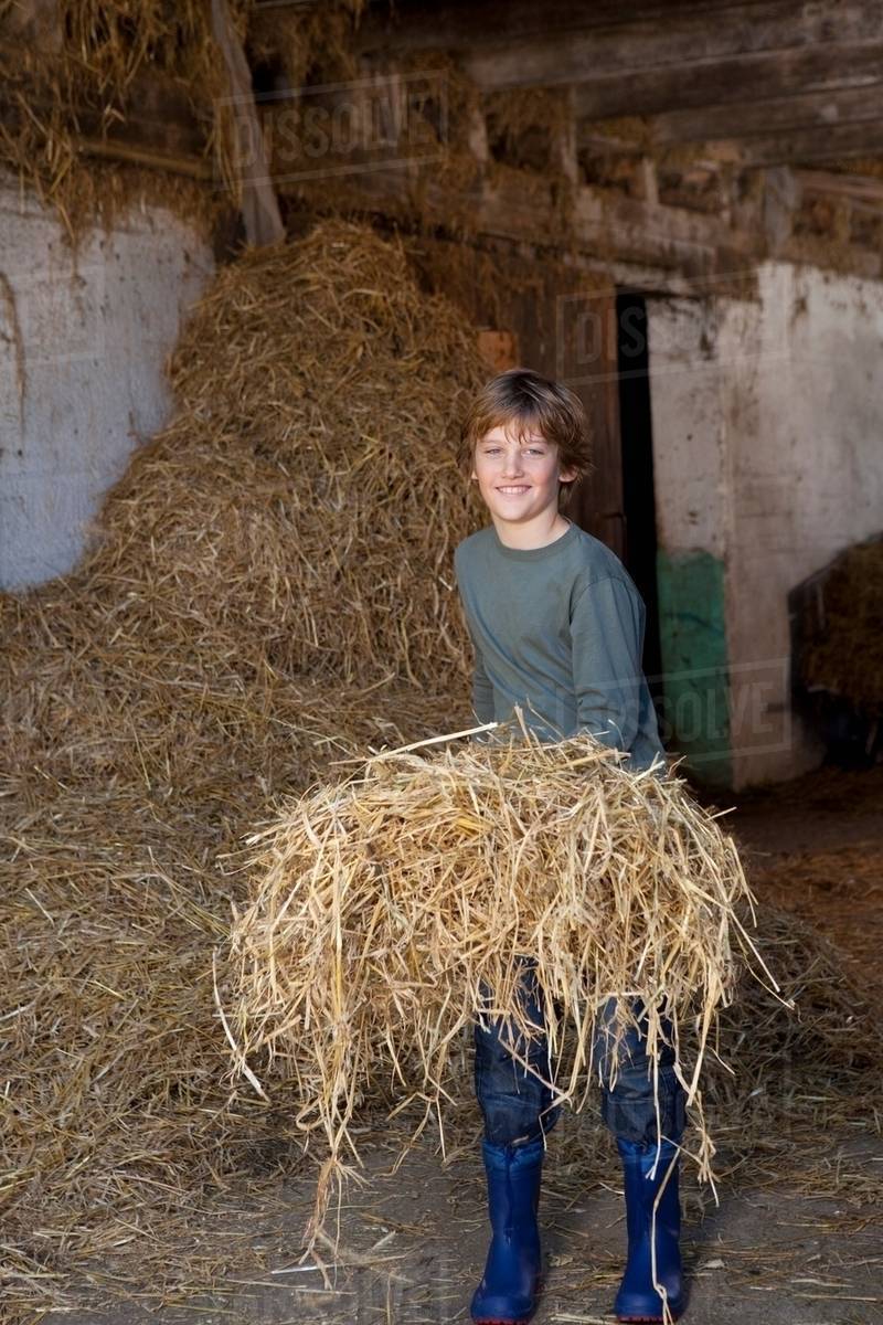 Boy with hay on fork, smiling - Stock Photo - Dissolve