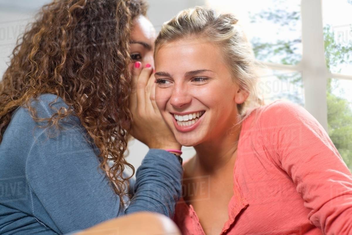 Young woman tell secret to friend in ear - Stock Photo - Dissolve