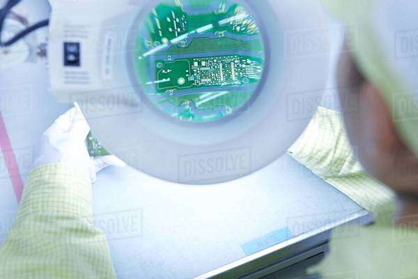 Young woman using magnifier at quality check station at factory ...