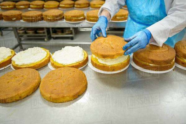 Female worker places top on cake in cake factory, close up - Stock ...