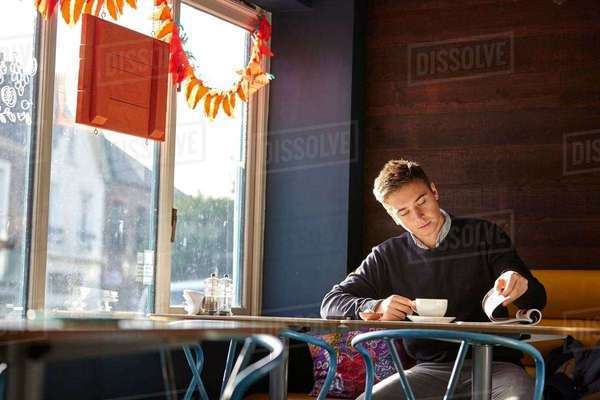 Young man alone in cafe drinking coffee and reading magazine - Royalty ...