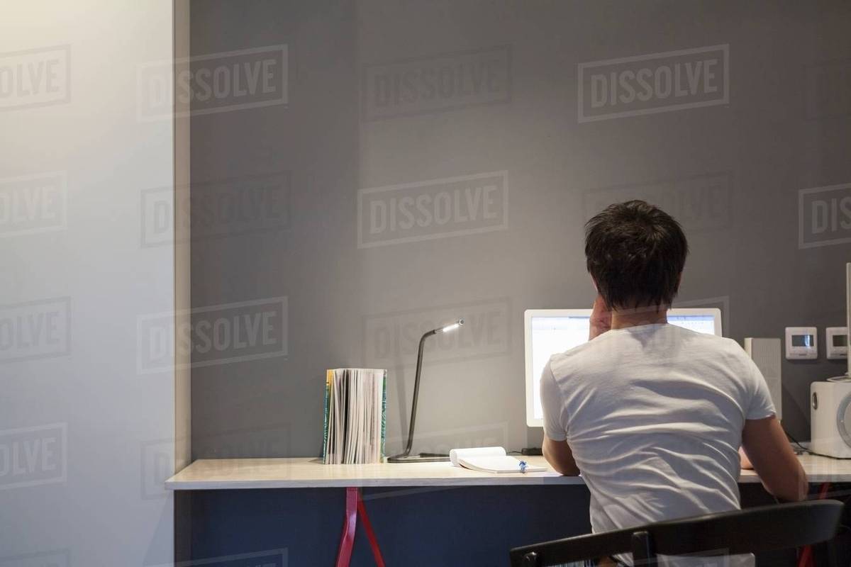 Rear view of man sitting at desk using desktop computer - Stock Photo ...