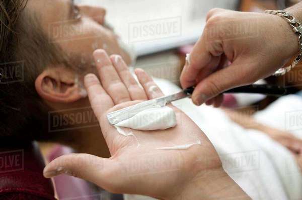 Barber wiping shaving cream from straight razor onto palm of hand ...