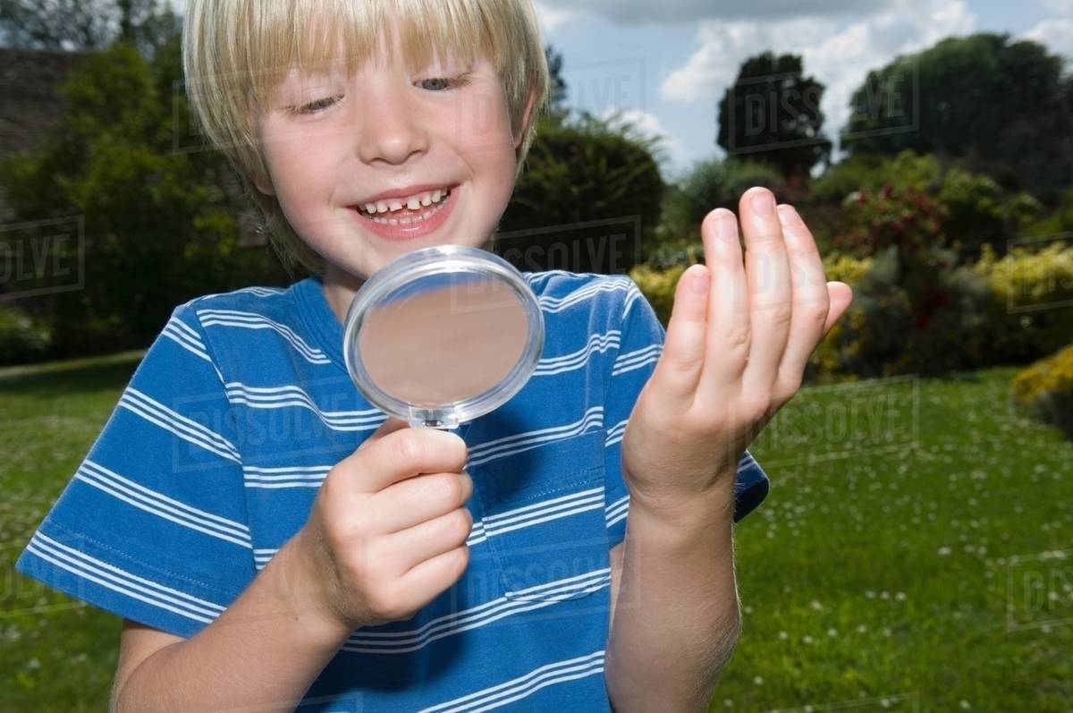 Boy using magnifying glass outdoors - Royalty-free Stock Photo | Dissolve