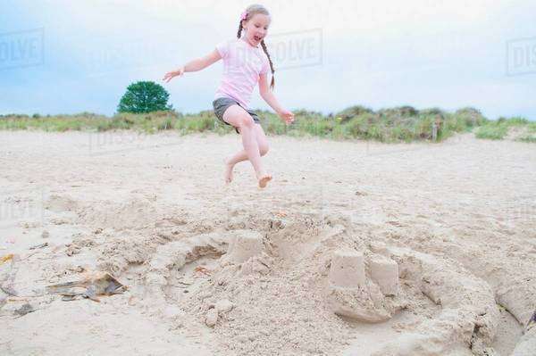 Girl destroying sand castle on beach - Royalty-free Stock Photo | Dissolve