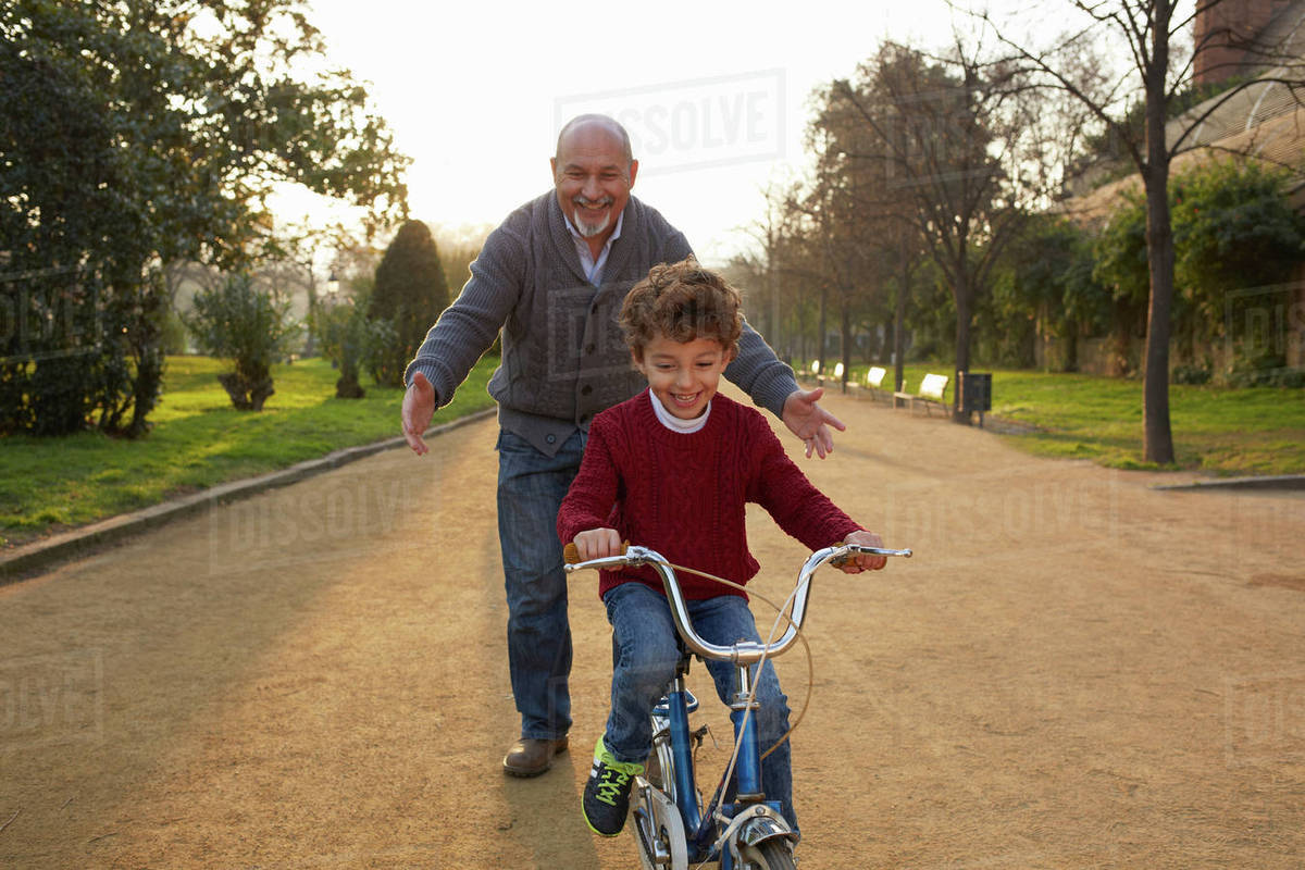 Grandfather teaching grandson to ride bicycle in park - Stock Photo ...