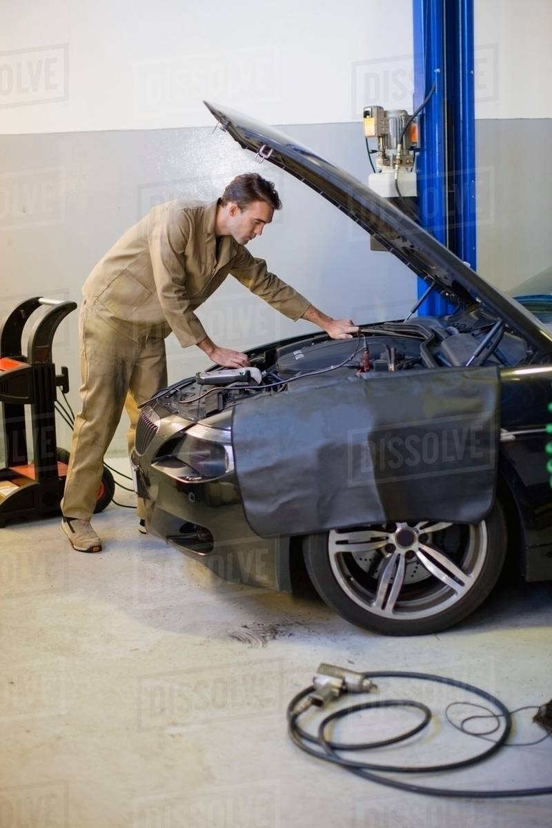 Mechanic working on car engine in garage - Stock Photo - Dissolve