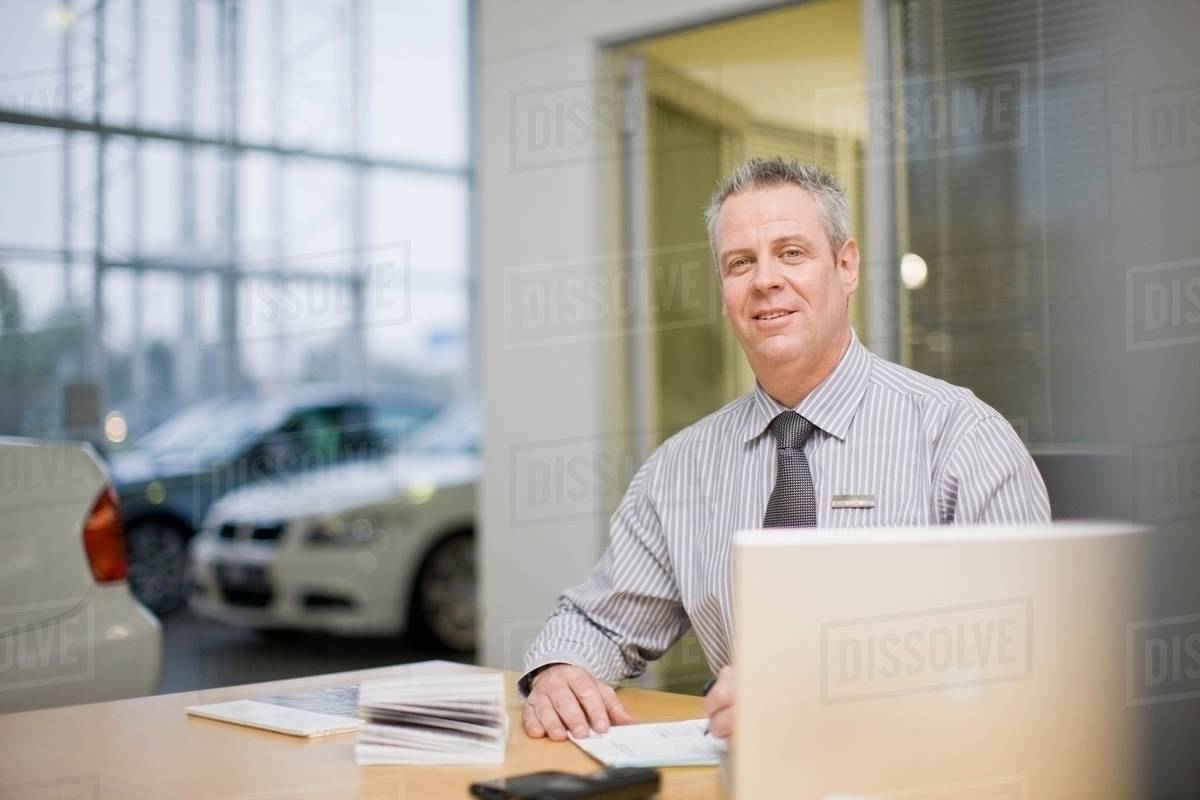 Car salesman sitting at desk in showroom - Royalty-free Stock Photo ...