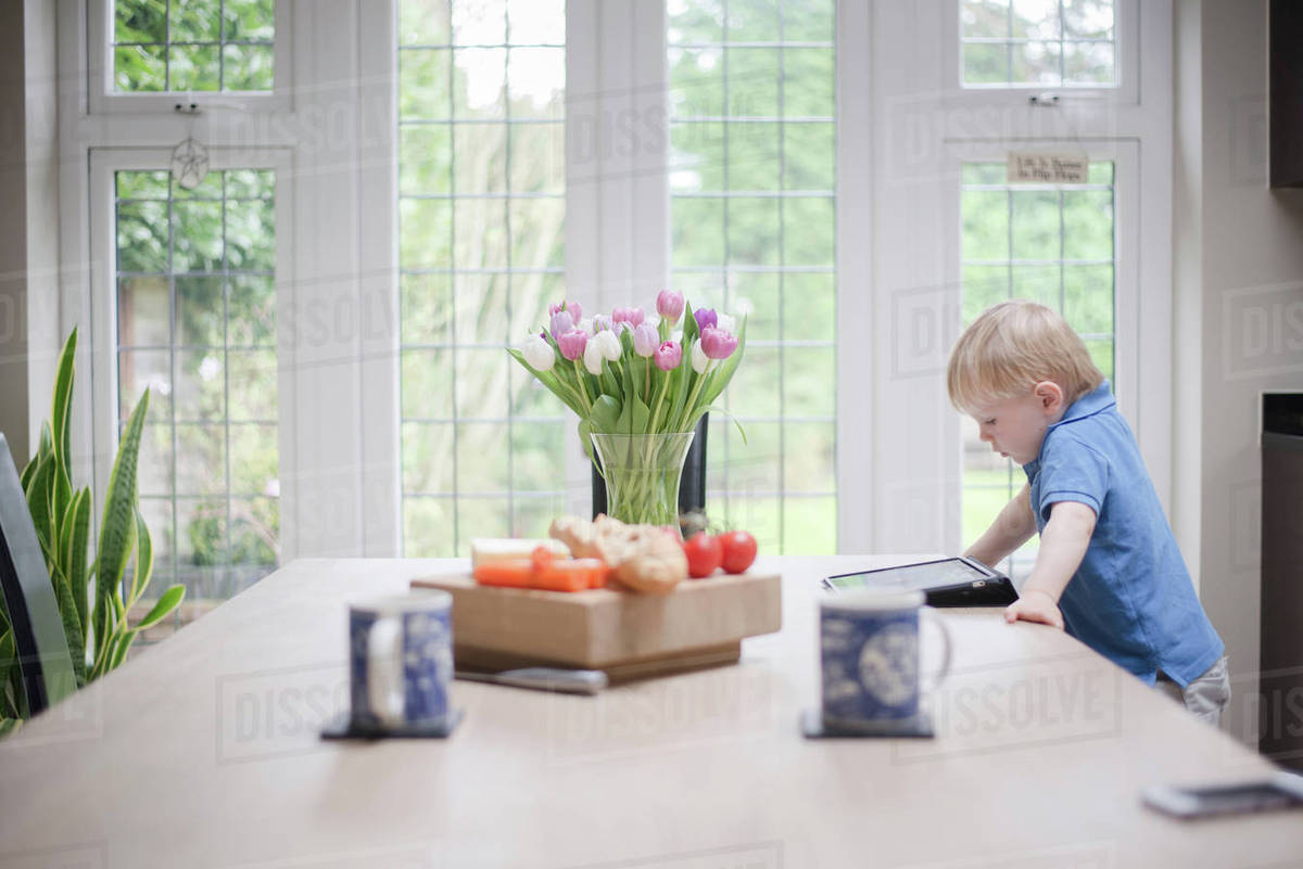 Young boy standing at table looking at digital tablet - Royalty-free ...
