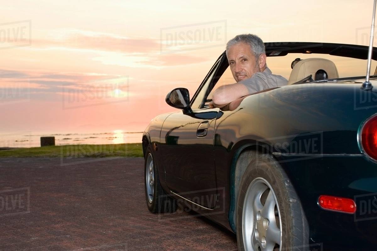 Man sitting in convertible on coastline - Royalty-free Stock Photo ...