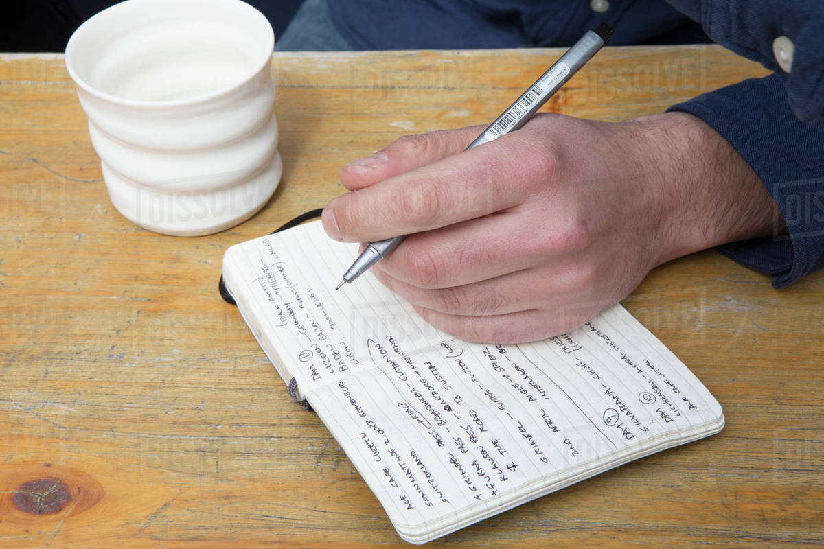 Hand of man at cafe table writing in note book - Stock Photo - Dissolve