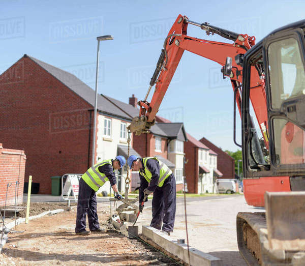 Builders using digger to lift kerb stones on housing building site ...