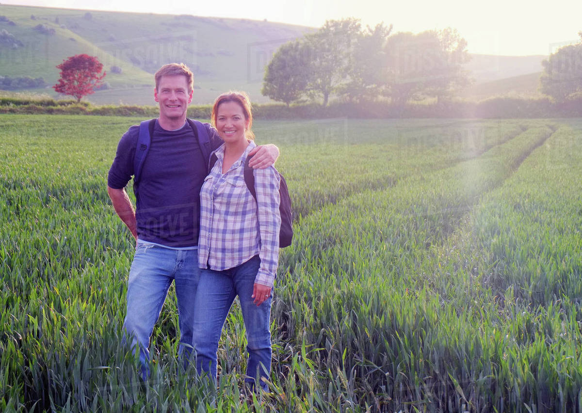 Couple in field looking at camera smiling - Stock Photo - Dissolve