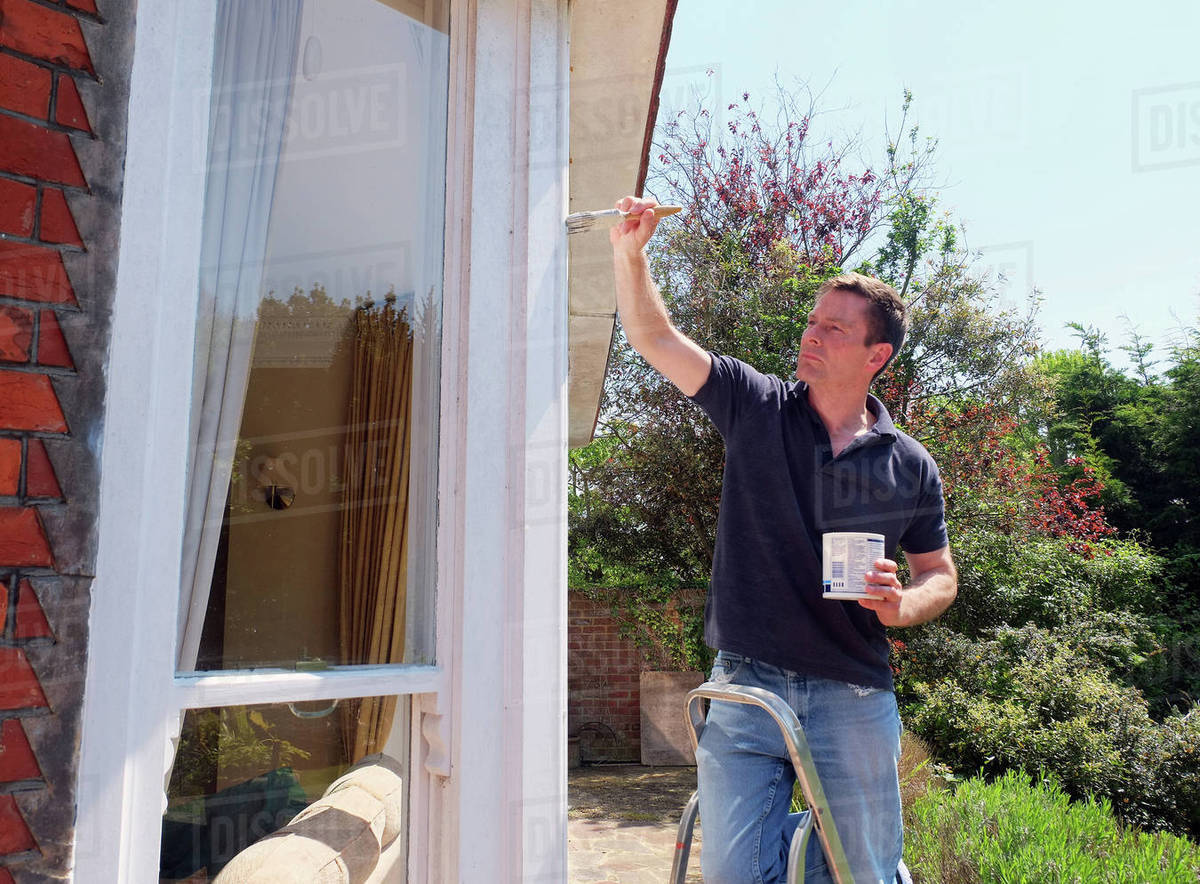 Man on ladder painting window frame - Stock Photo - Dissolve