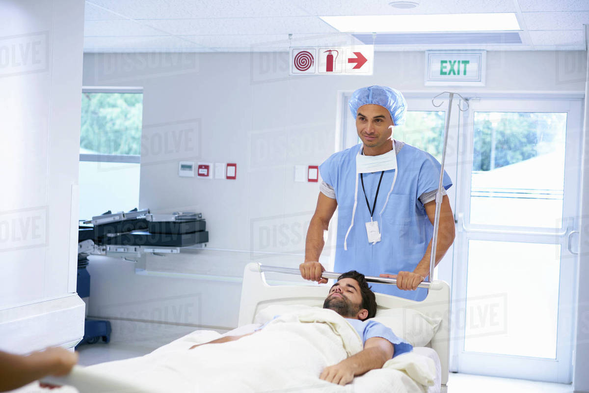 Doctors wearing surgical scrubs pushing patient on hospital bed ...