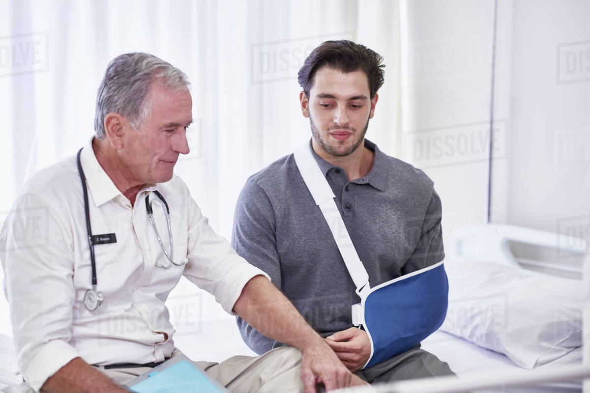 Doctor and man with arm in sling sitting on hospital bed - Stock Photo ...