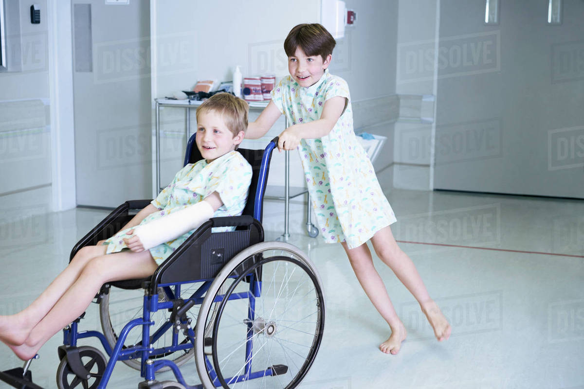 Boy patients pushing friend in wheelchair on hospital children's ward ...