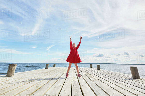 Young girl on wooden pier, jumping to reach bubbles - Stock Photo ...