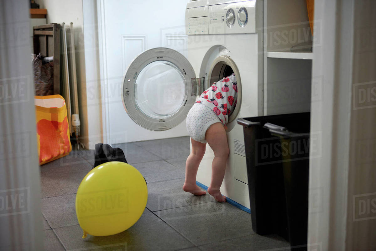 Baby girl investigating inside washing machine - Stock Photo - Dissolve