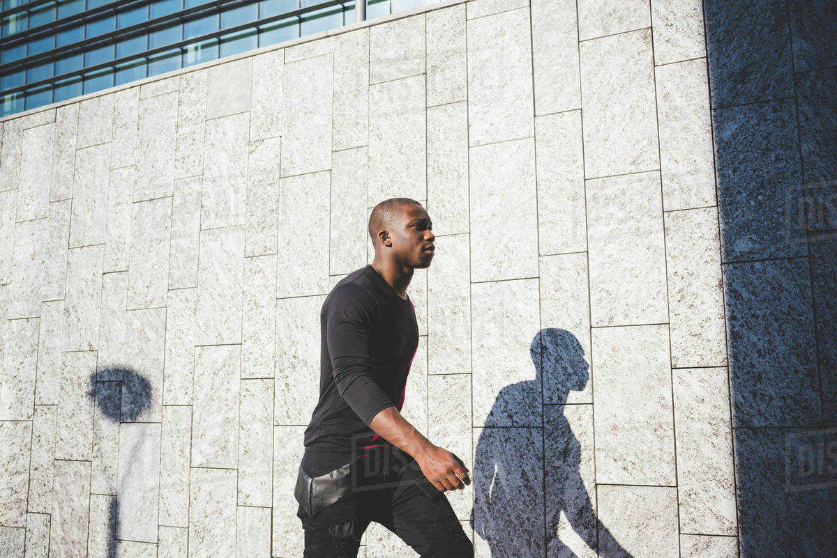 Young man walking outdoors, shadow cast on wall beside him - Royalty ...