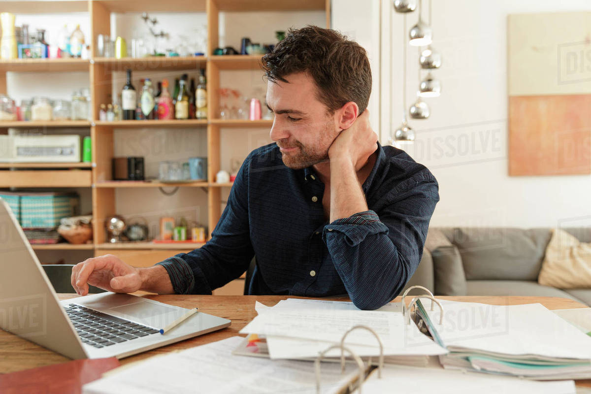 Man with laptop looking at paperwork - Royalty-free Stock Photo | Dissolve
