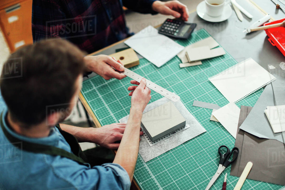 Young craftsman passing metal ruler to friend in print studio, elevated ...