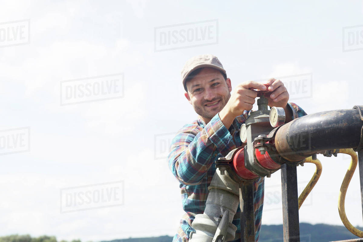 Man opening valve on industrial piping, looking at camera smiling ...