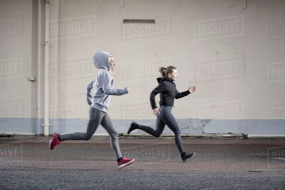 Two female runner friends running on urban road - Stock Photo - Dissolve